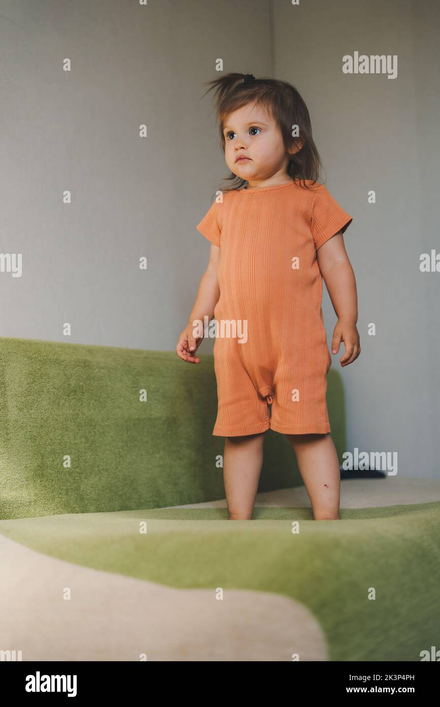 Portrait of adorable baby girl standing on soft sofa and looking away ...