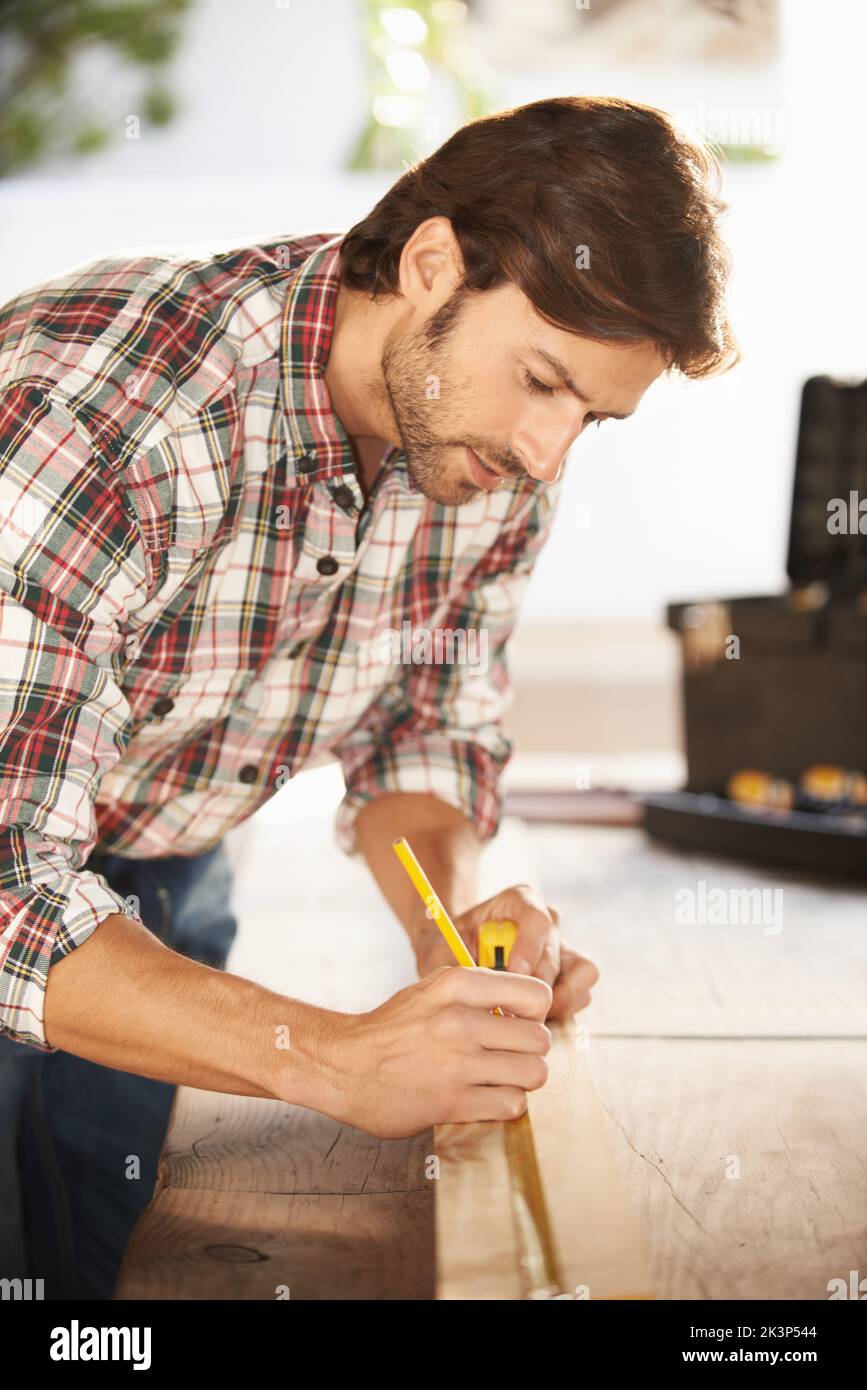 Home DIY. A handsome young carpenter taking measurements of some wood ...