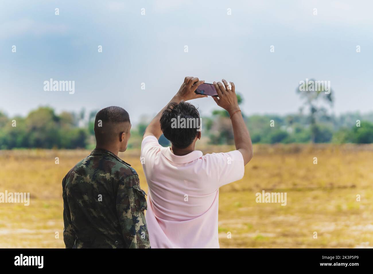 Back view of Asian man using cell phone to take sky photo with army ...