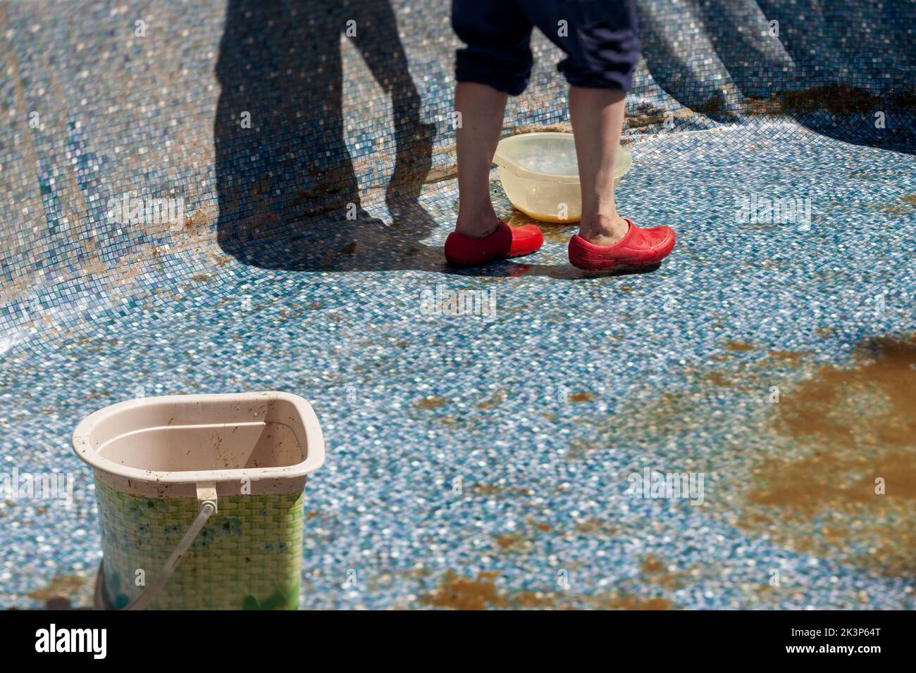 female cleaner standing on the bottom of empty outdoor pool, sunny day ...
