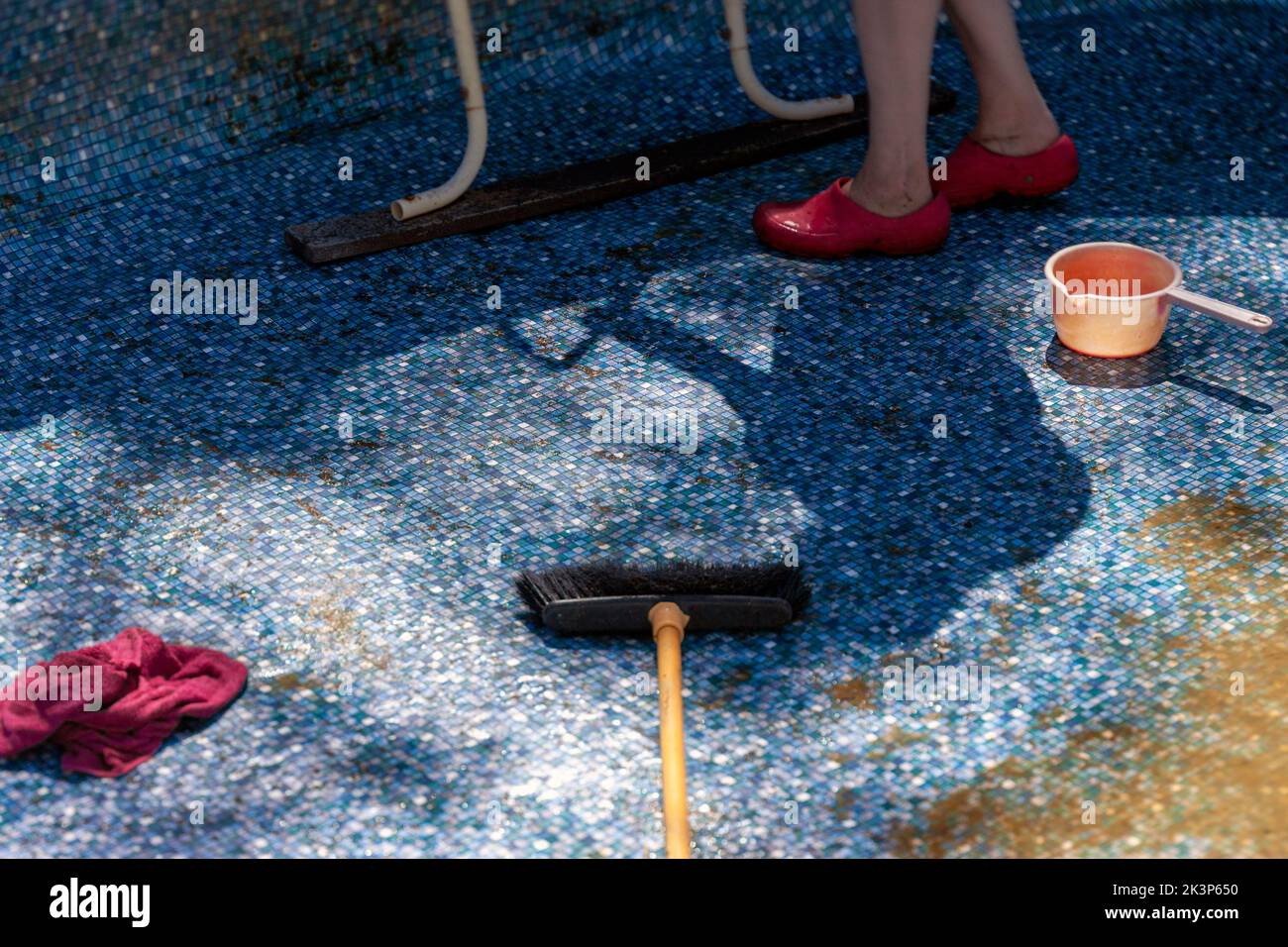 female wearing rubber boots cleaning above ground pool, sunny day shot ...