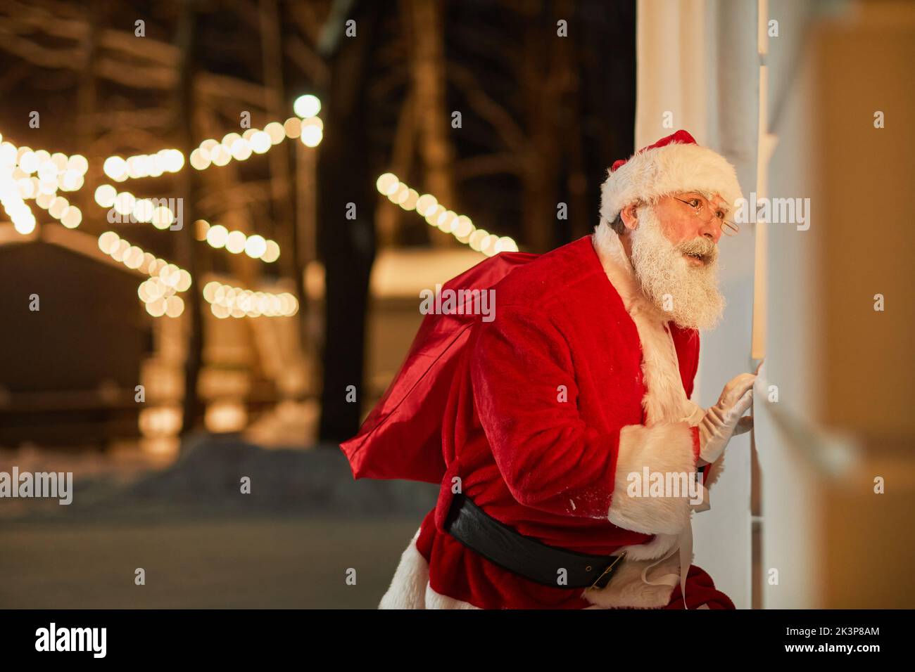 Side view portrait of classic Santa Claus looking in house windows at ...