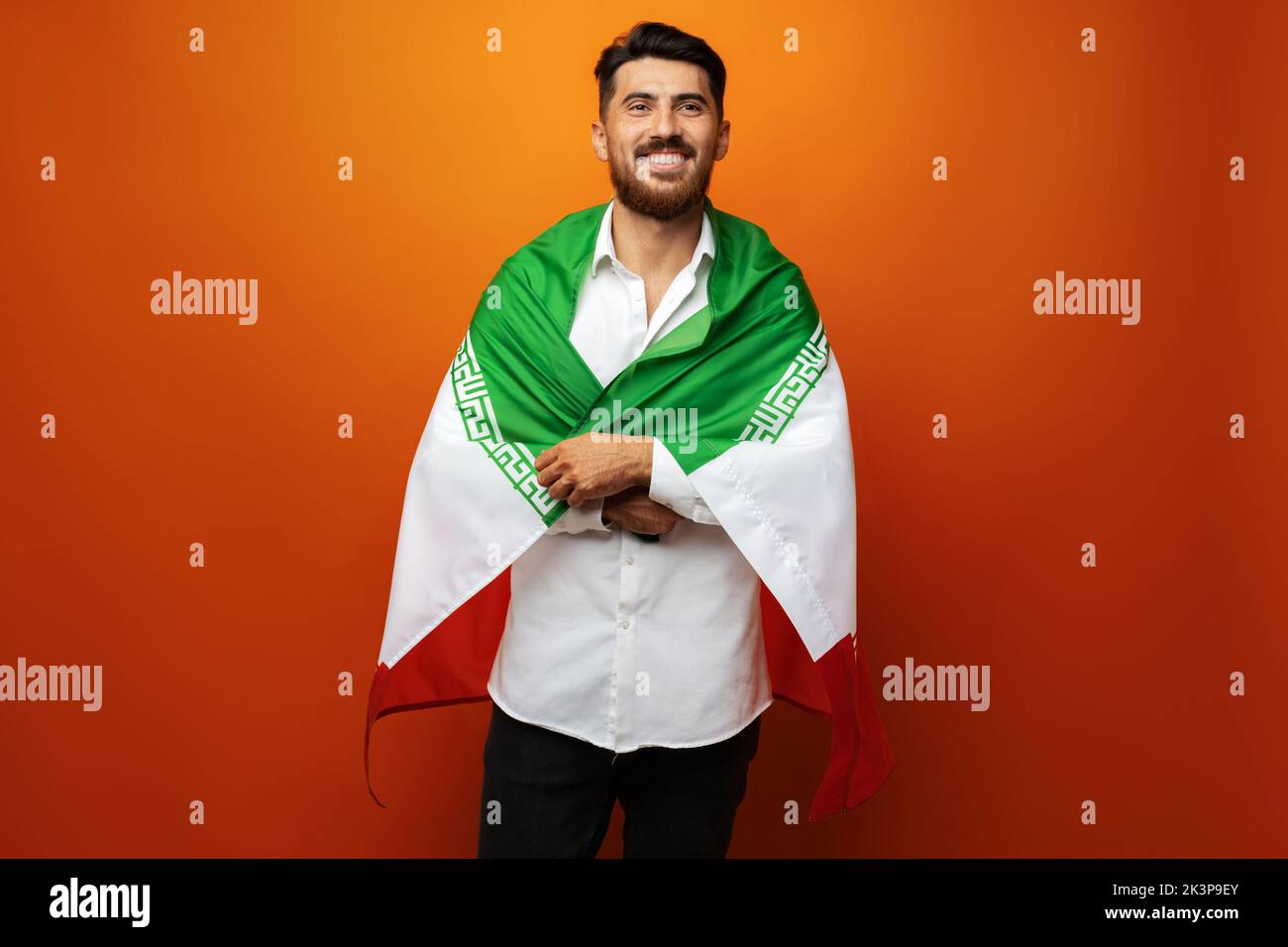 Portrait of a young casual man holding flag of Iran against orange ...