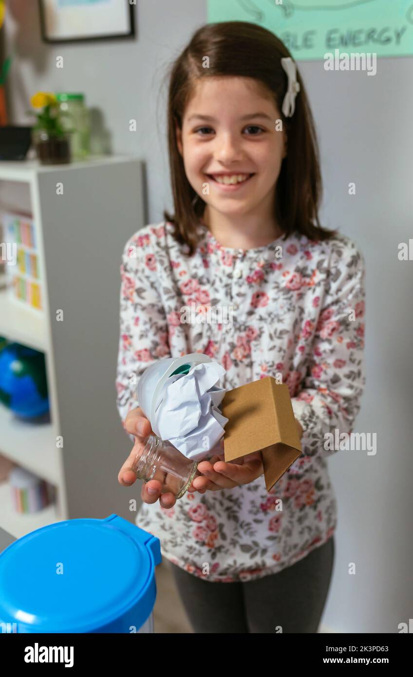 Smiling girl in an ecology classroom showing a handful of waste to ...