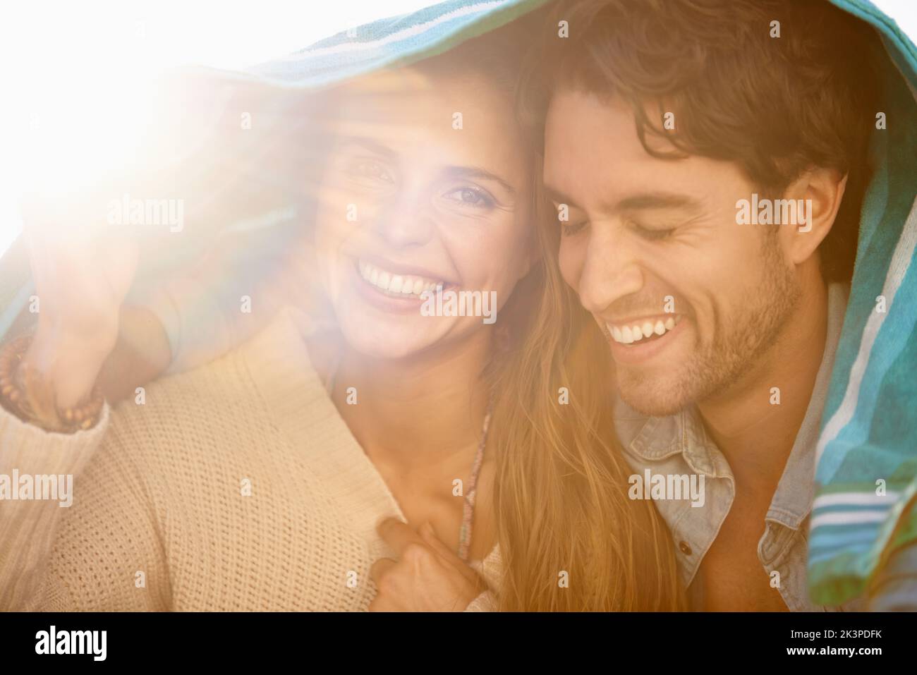 Safely wrapped in our love. A young couple smiling and cuddling under a ...