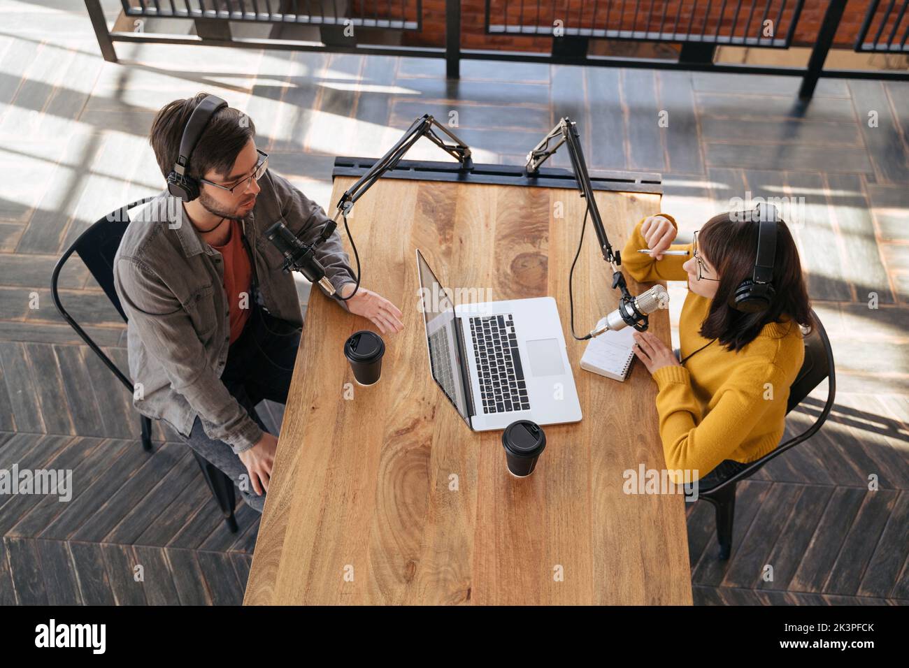 Two young radio hosts in headphones are talking while sitting near ...