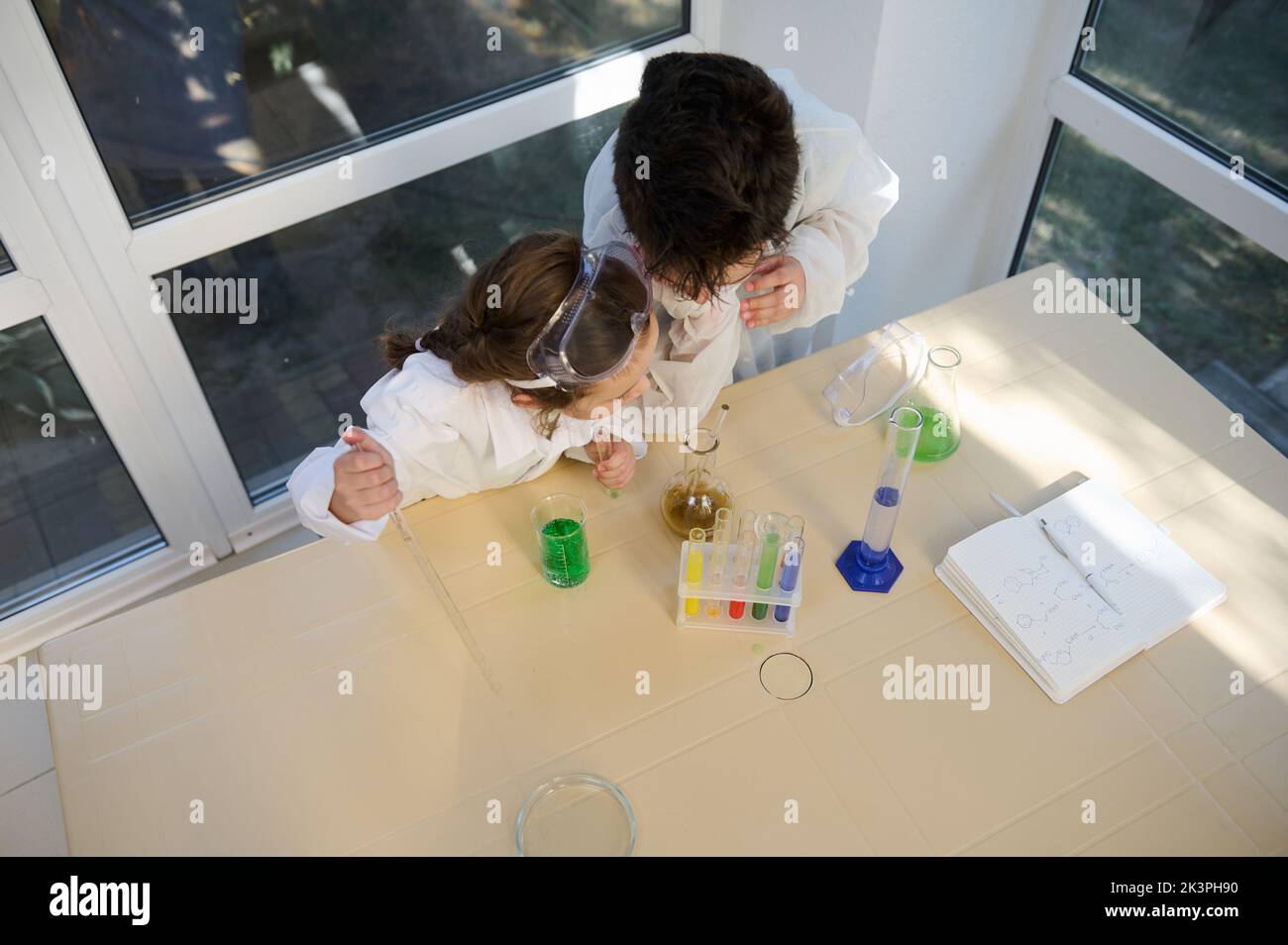 Overhead view of school kids in safety goggles and white lab coat ...