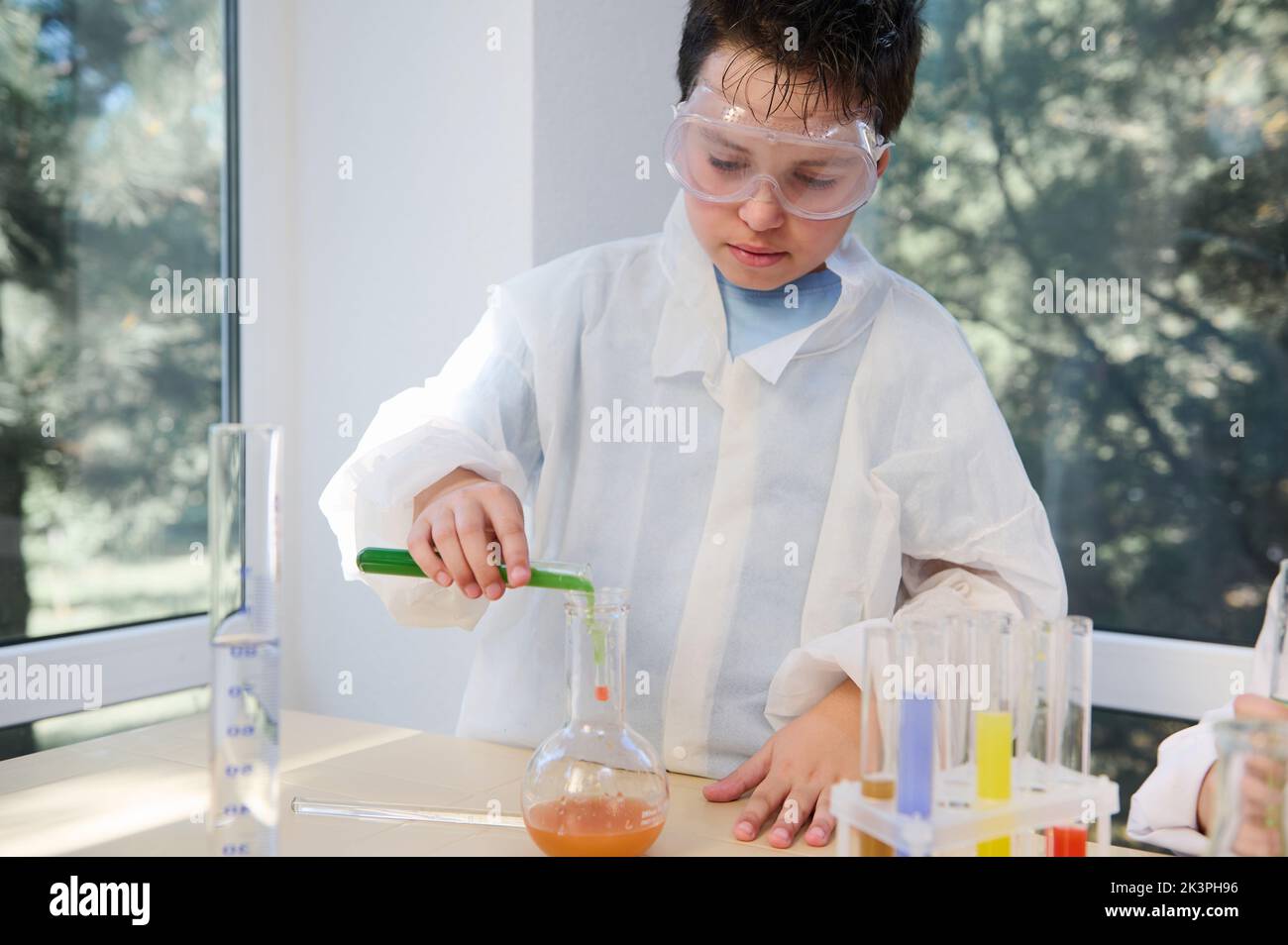Smart schoolboy pours chemical liquid from test tube into a glass flask ...