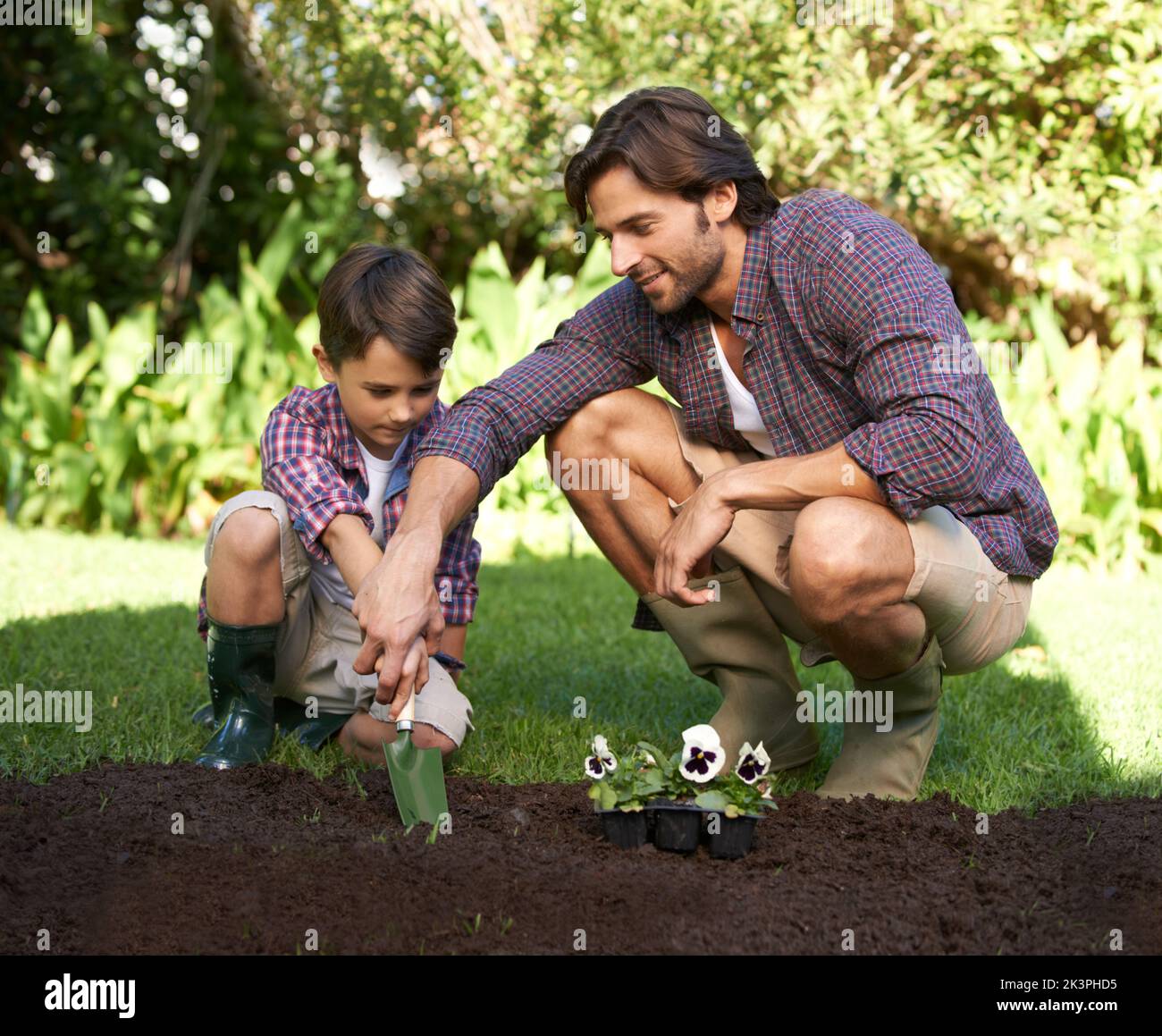 Showing him the ways of the gardener. a father and son planting flowers ...