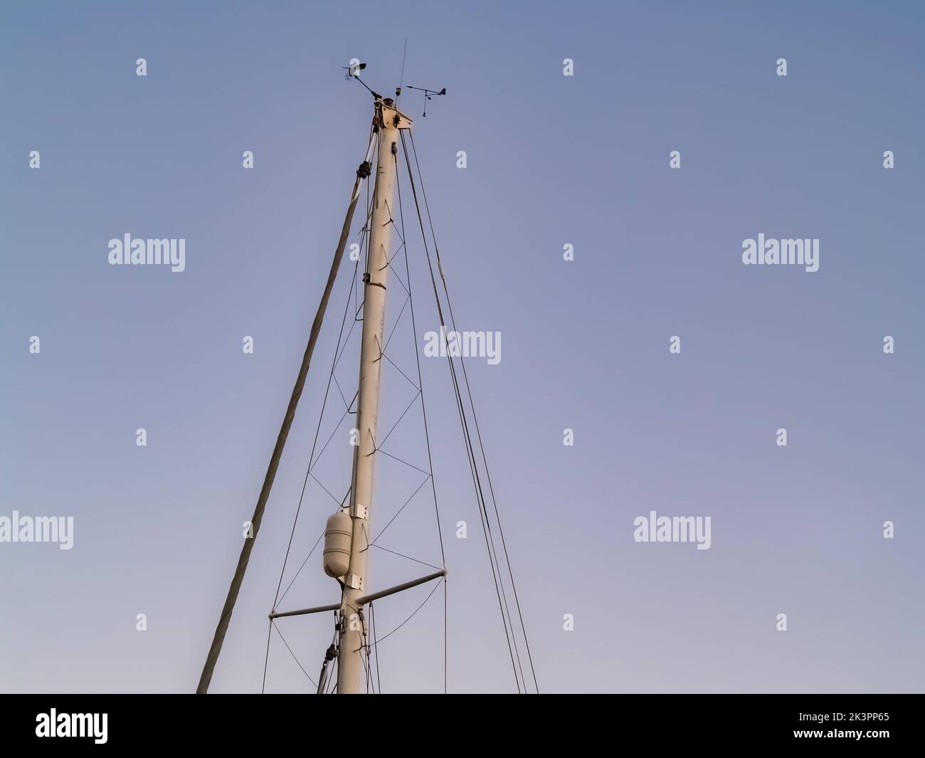 Yacht mast with rigging, stays and wind indicator on top against blue ...