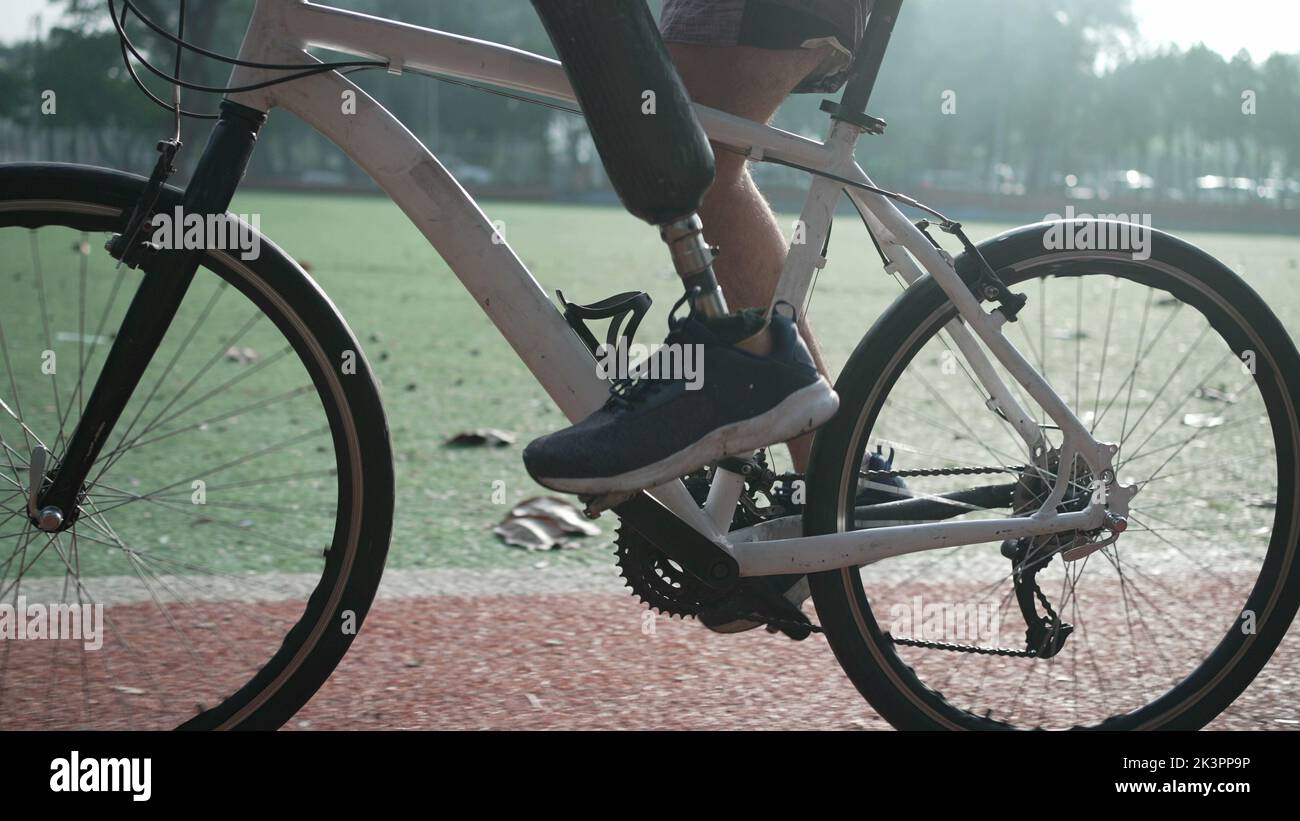 Person with prosthetic leg riding bicycle outdoors. A disabled athlete ...