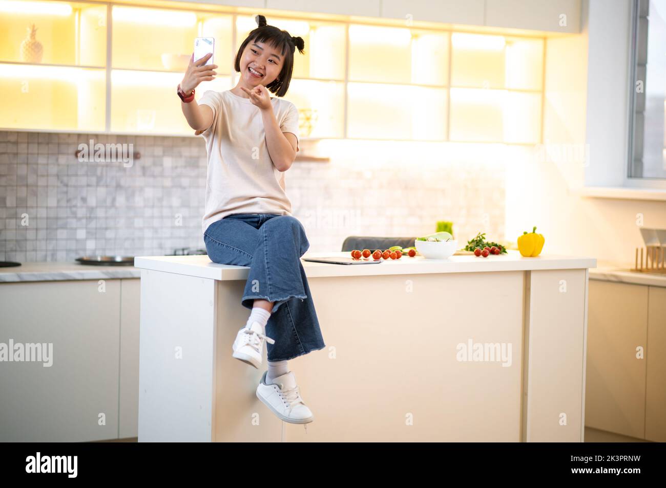 Mischievous girl photographing herself seated in the kitchen counter ...