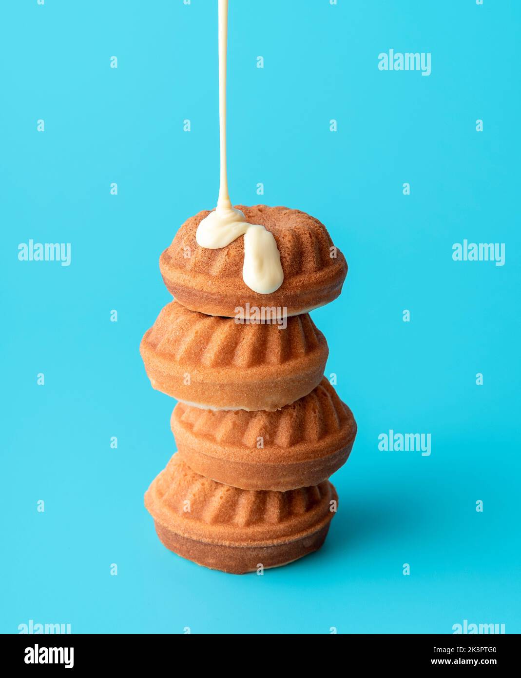 Homemade miniature sponge cakes in a stack on a blue table. Pouring ...