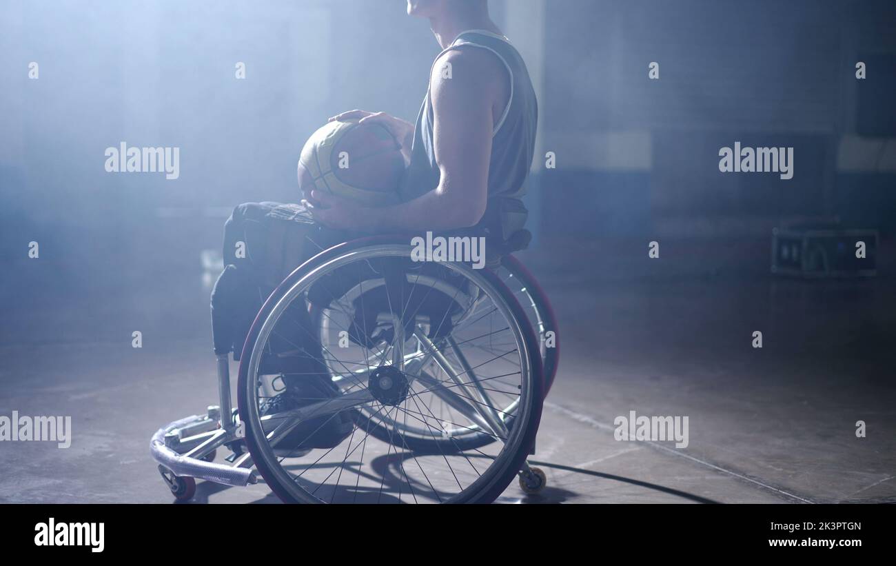 Disabled athlete in a wheelchair with dramatic lighting holding ball ...