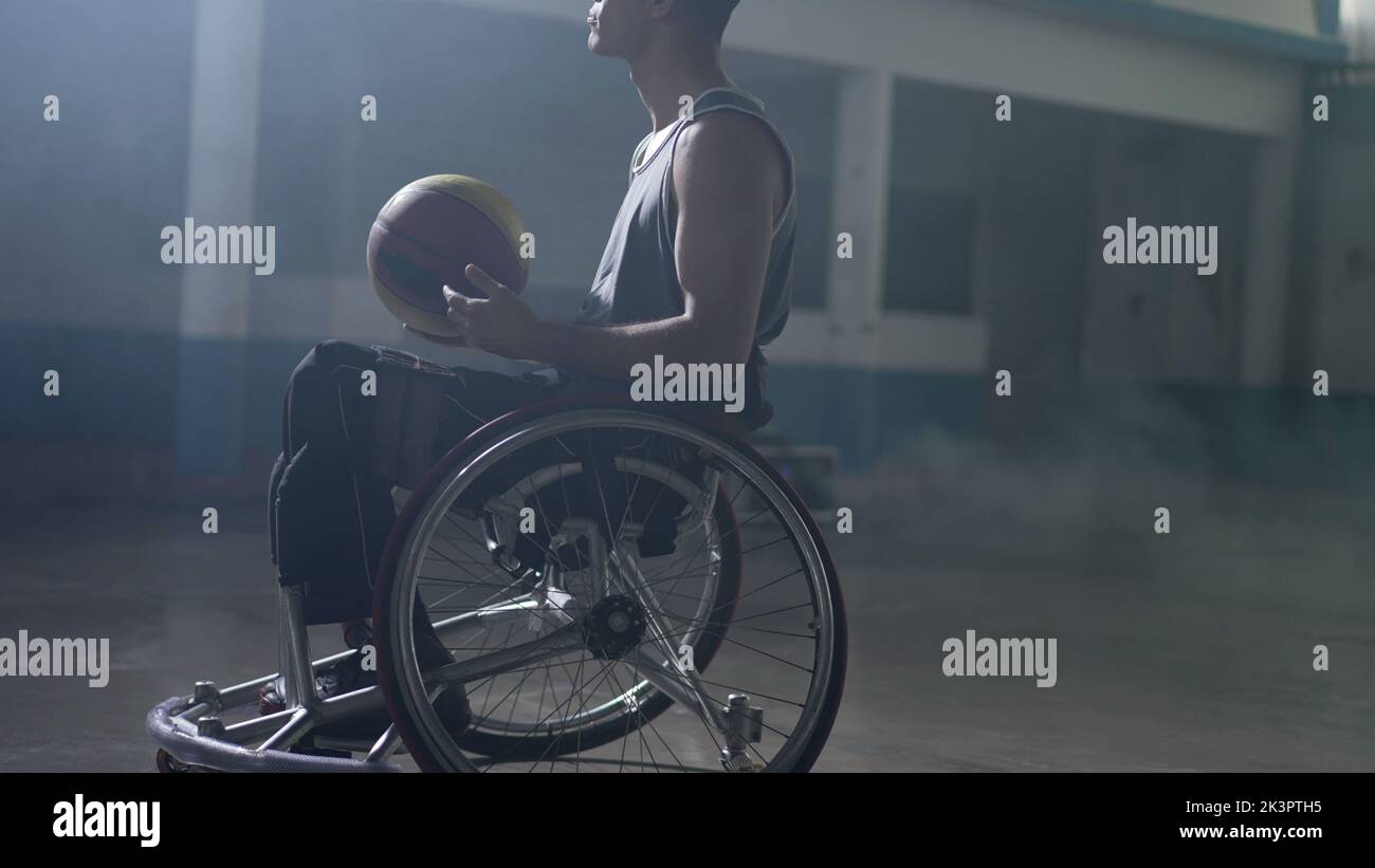 Disabled athlete in a wheelchair with dramatic lighting holding ball ...