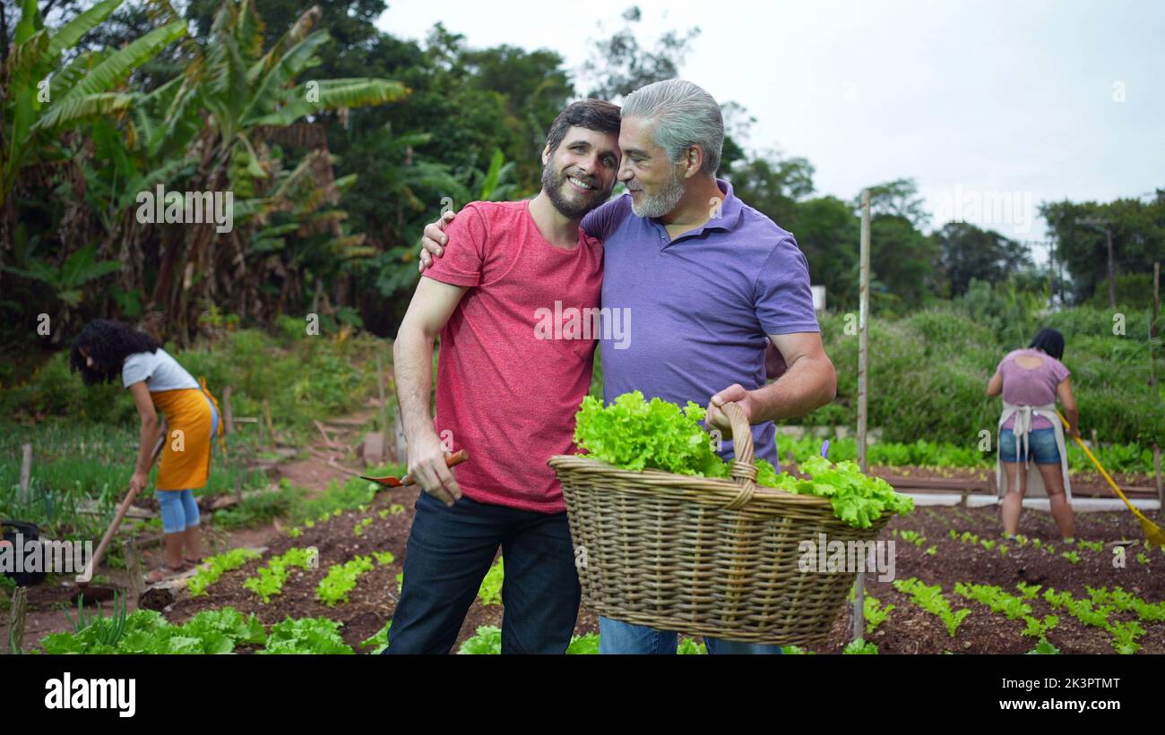 Father and son standing at small local farm holding organic lettuces ...
