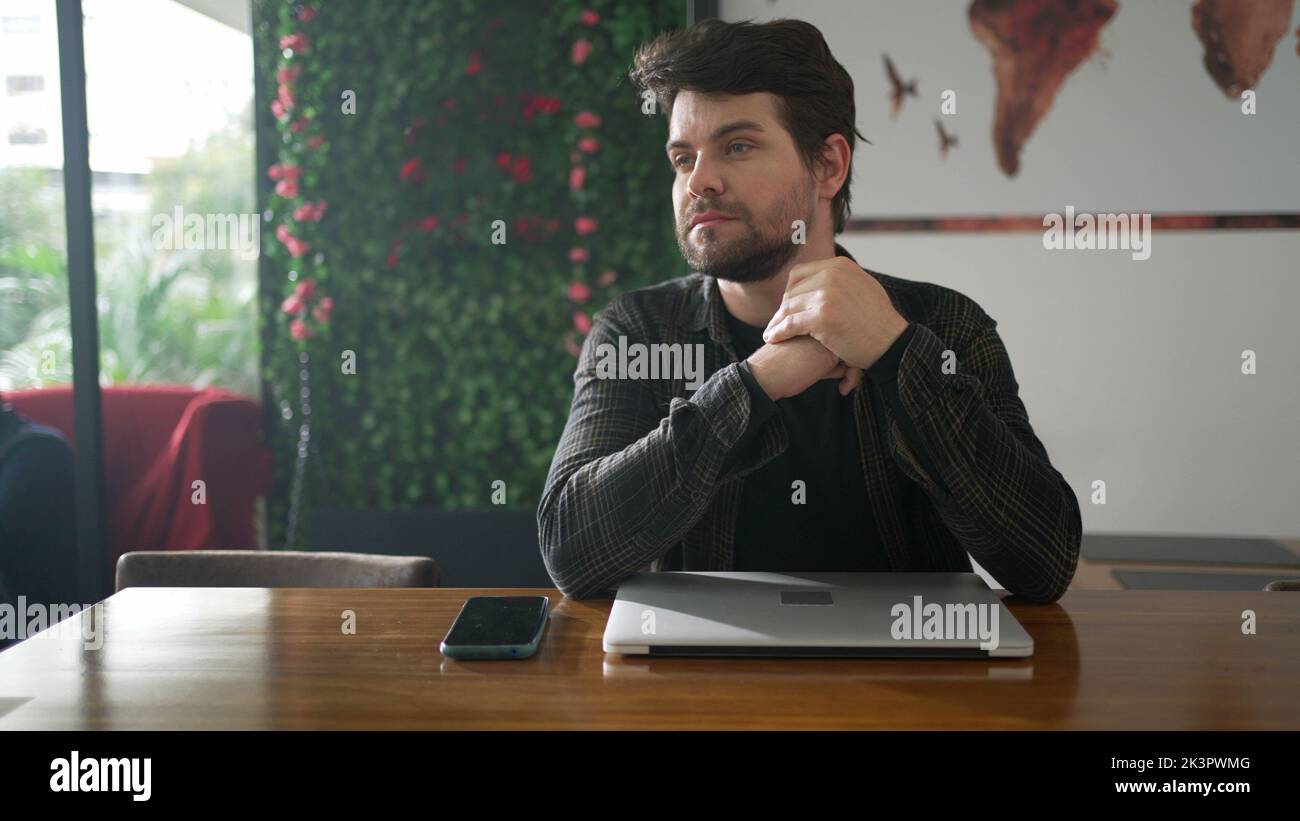 Thoughtful young man sitting at coffee shop with serious expression. Concentrated person ...