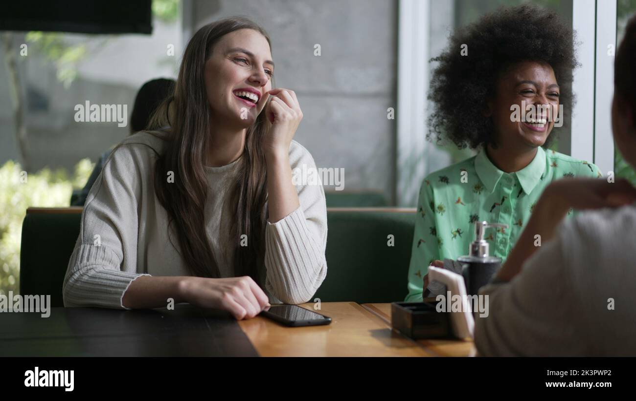 Three young diverse women laughing and smiling sitting at coffee shop ...