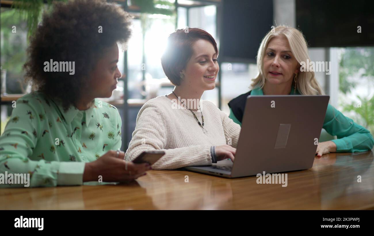 Three diverse women in front of laptop seated at coffee shop. Young ...