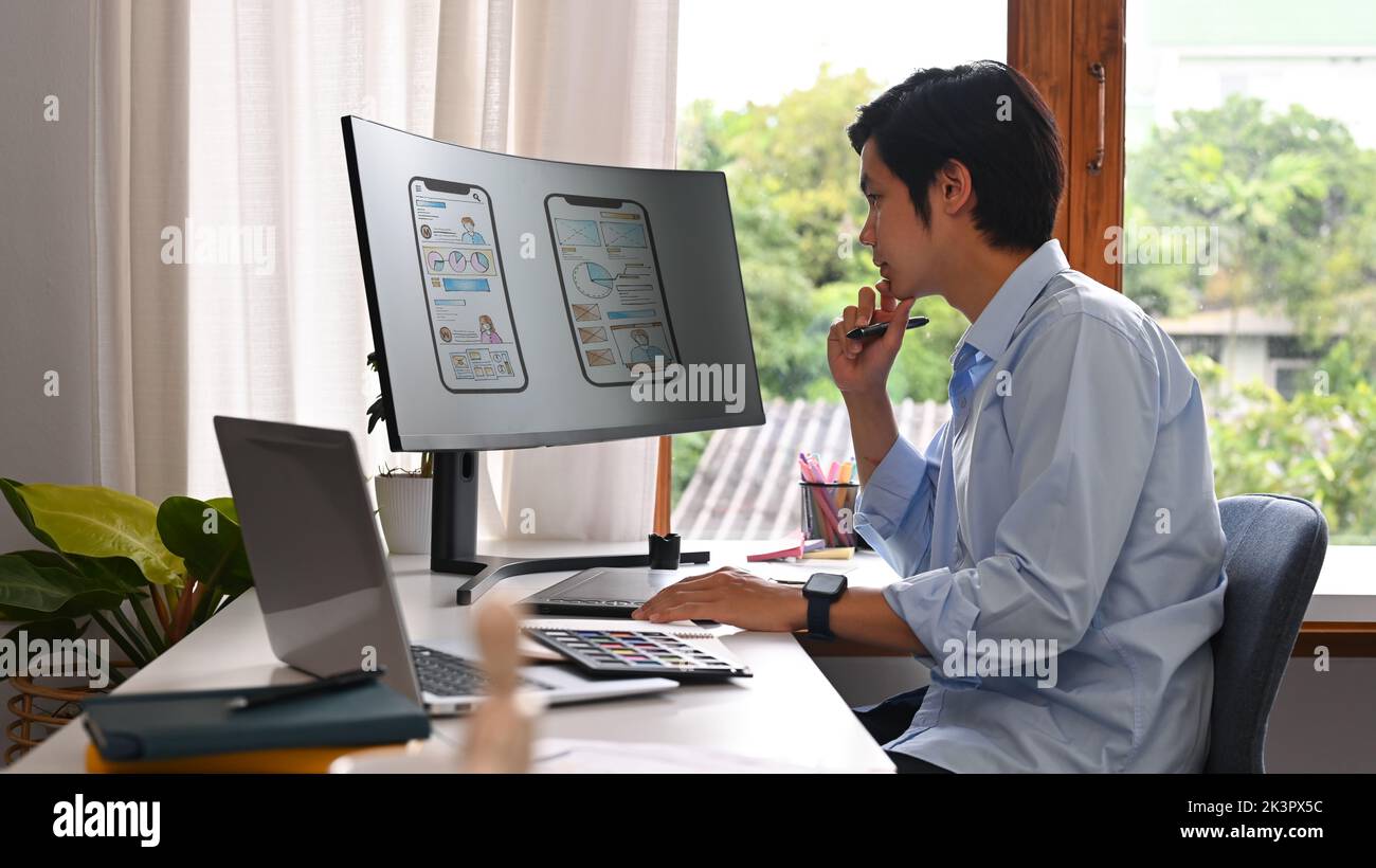 Concentred asian man developer working on mobile application software design project at modern ...