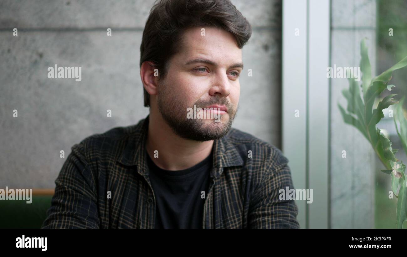 One pensive young man sitting by window looking at city. Thoughtful ...