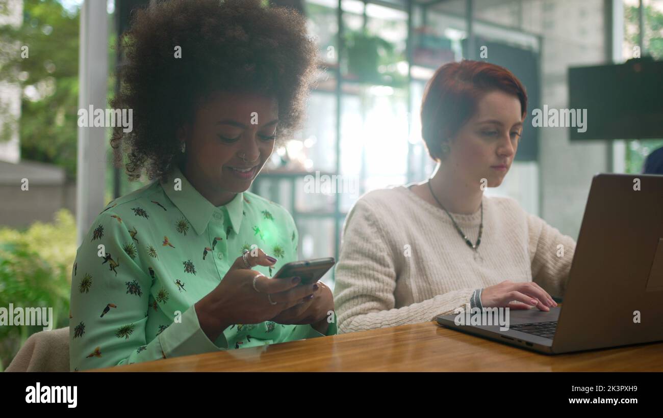 People using cellphone and laptop at coffee shop. Two young women ...