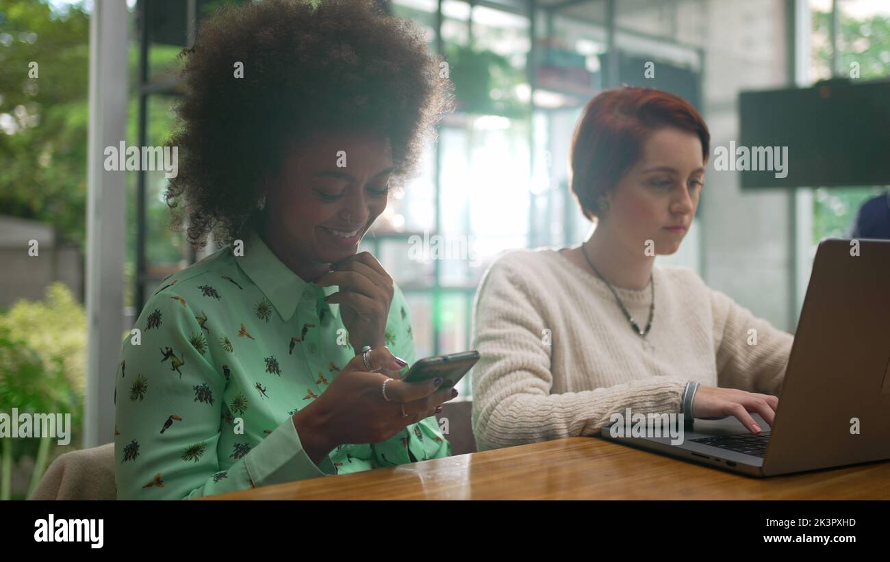 People using cellphone and laptop at coffee shop. Two young women ...