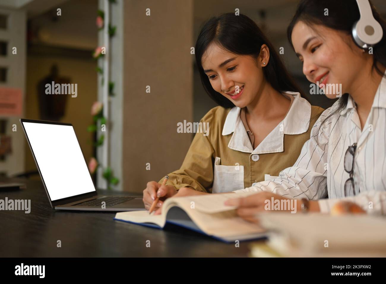 Two young asian woman doing class assignment together and using laptop ...