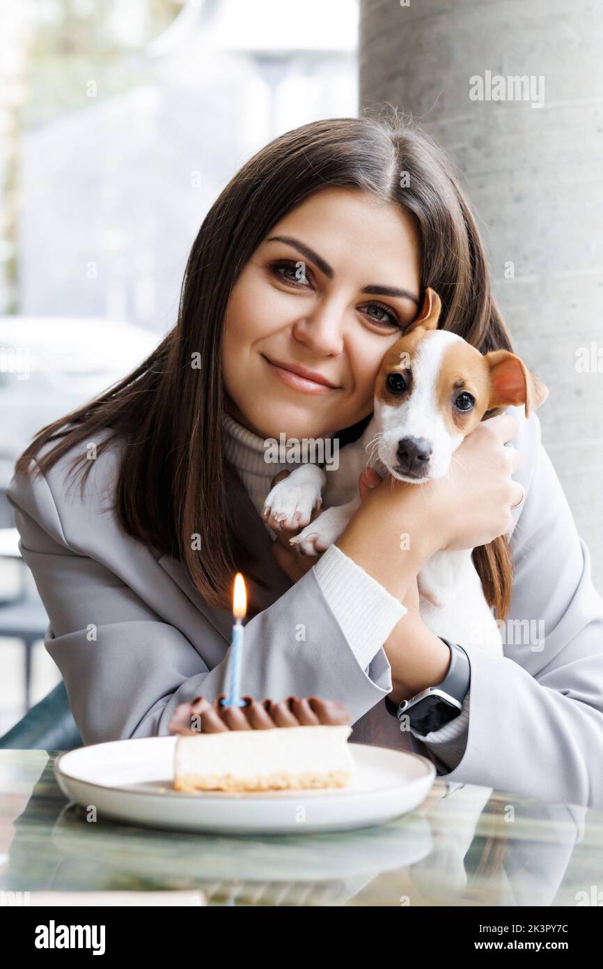 Caucasian woman and jack russell terrier look at the cake with a candle ...