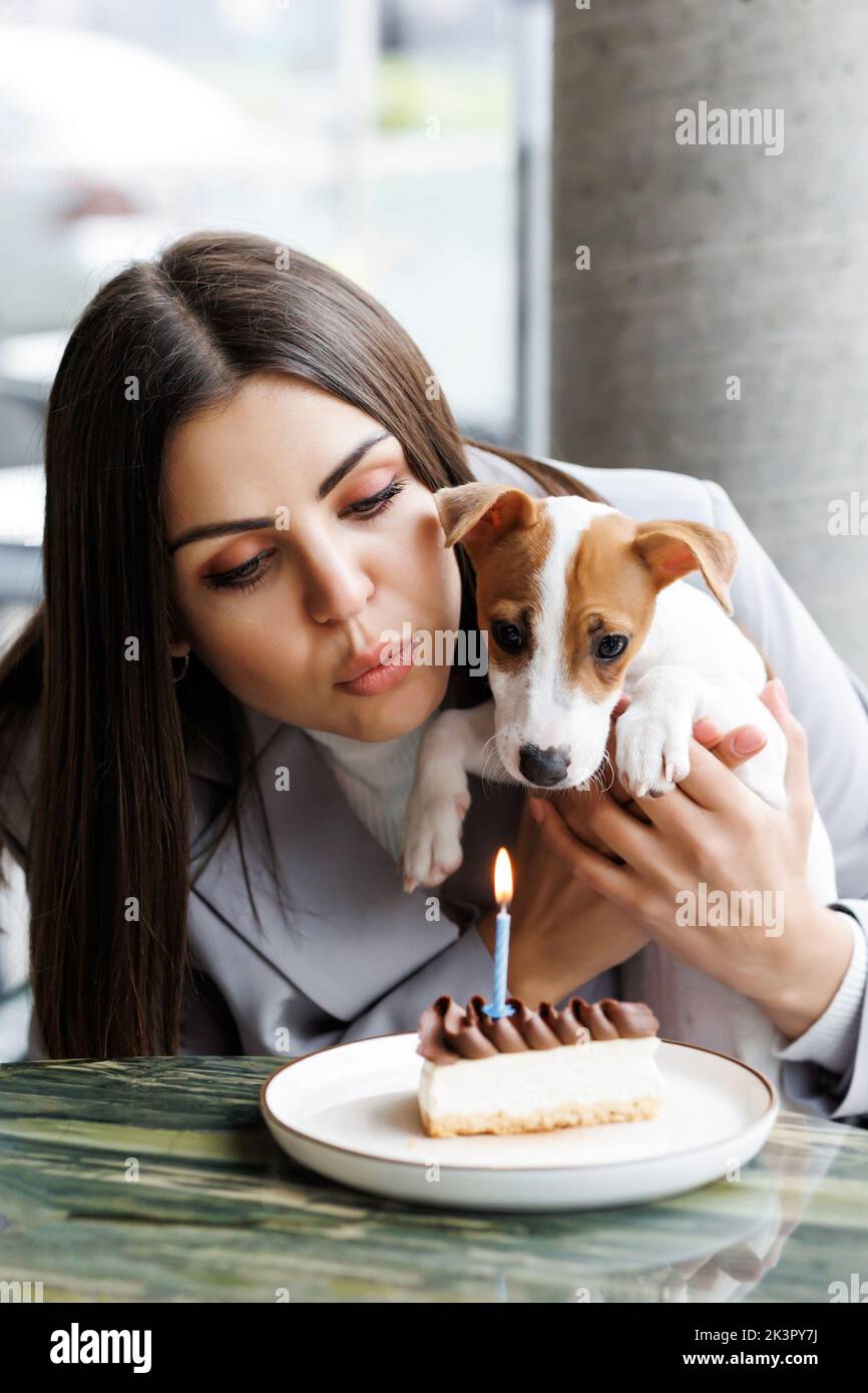 Caucasian woman and jack russell terrier look at the cake with a candle ...