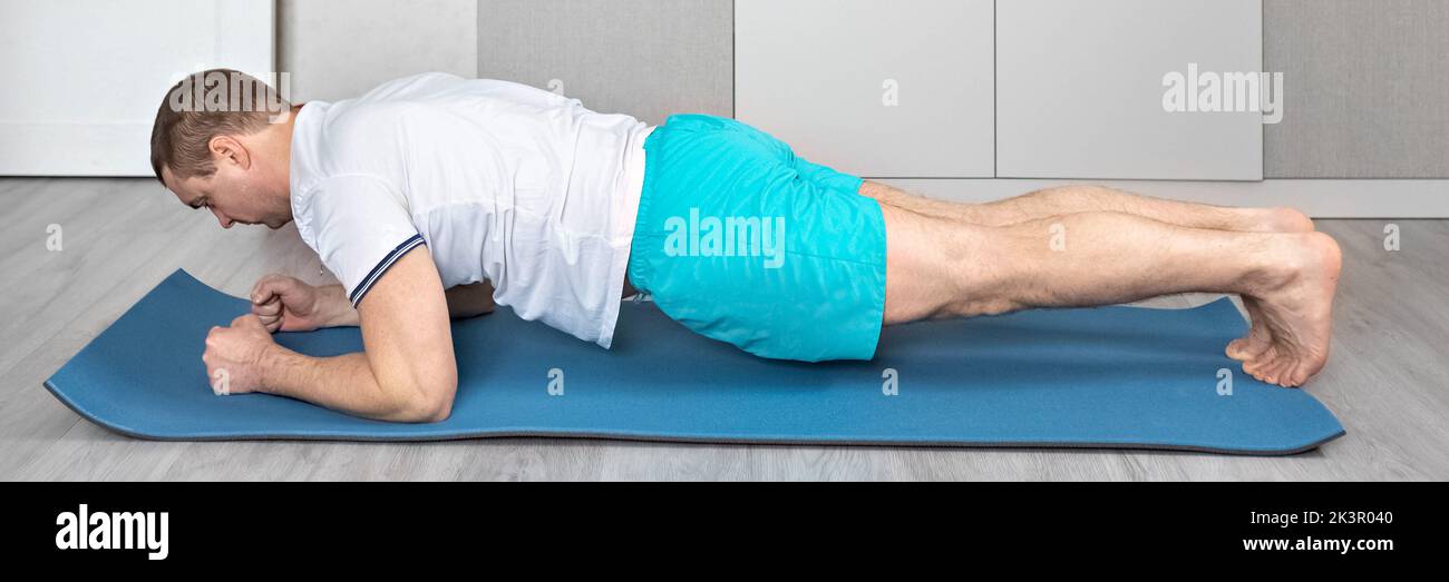 A strong, healthy man with muscles, training at home in the plank ...