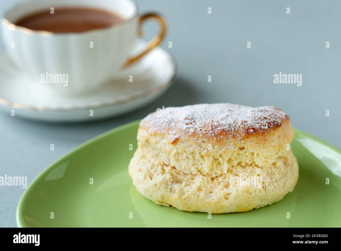 A freshly made traditional plain scone served on a plate with a cup of ...