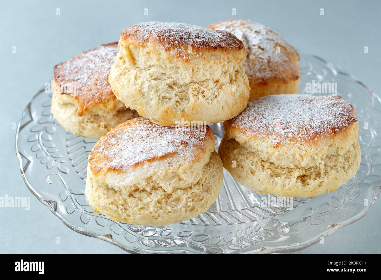 Freshly made traditional plain scones are shown on a glass cake stand ...