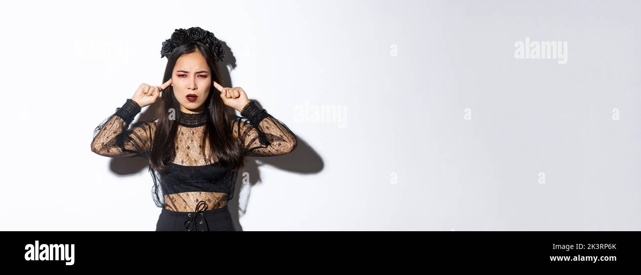Annoyed and mad asian woman in witch halloween costume shut ears and ...