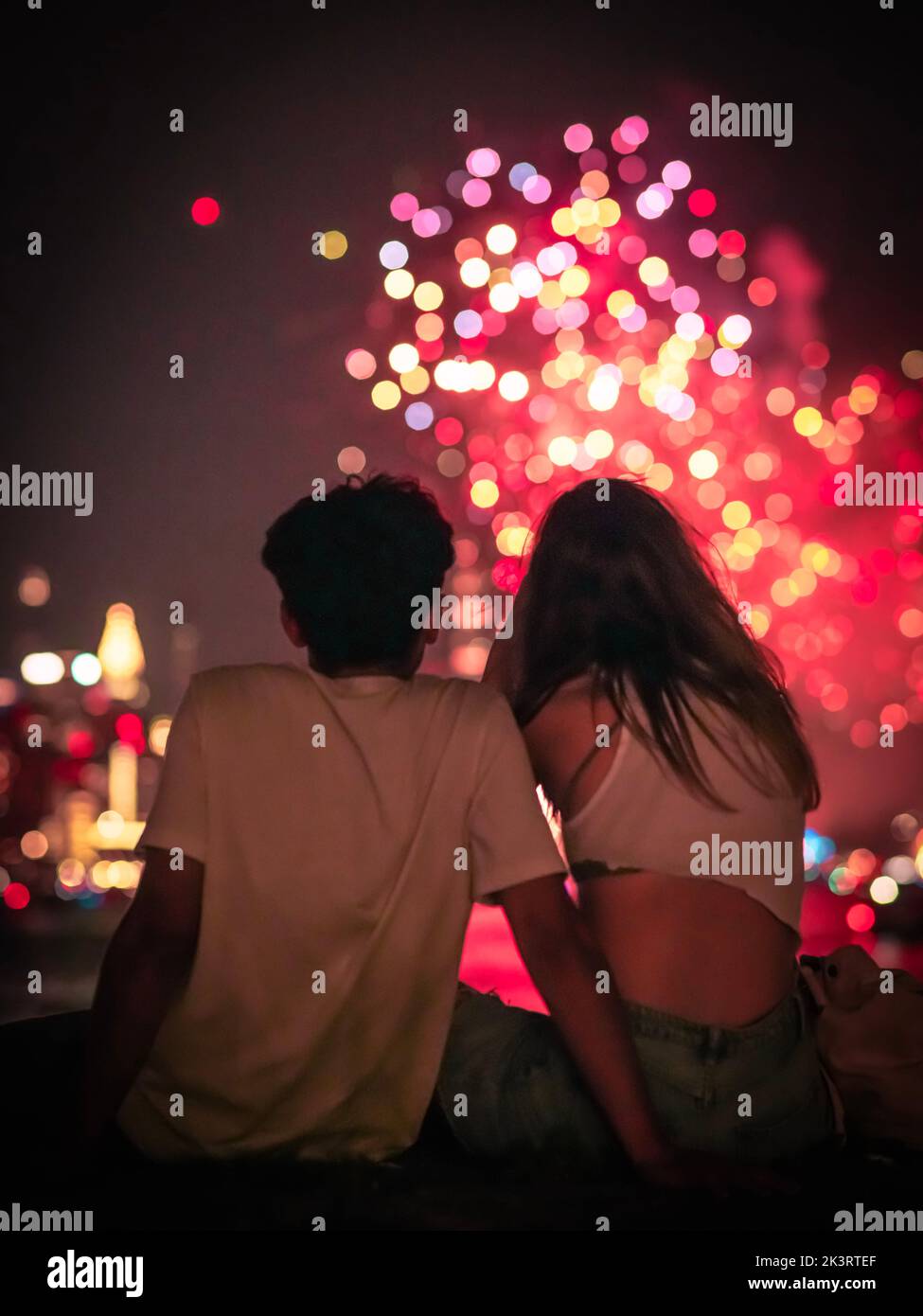 A vertical back view of a couple watching exploding bright red July 4th ...