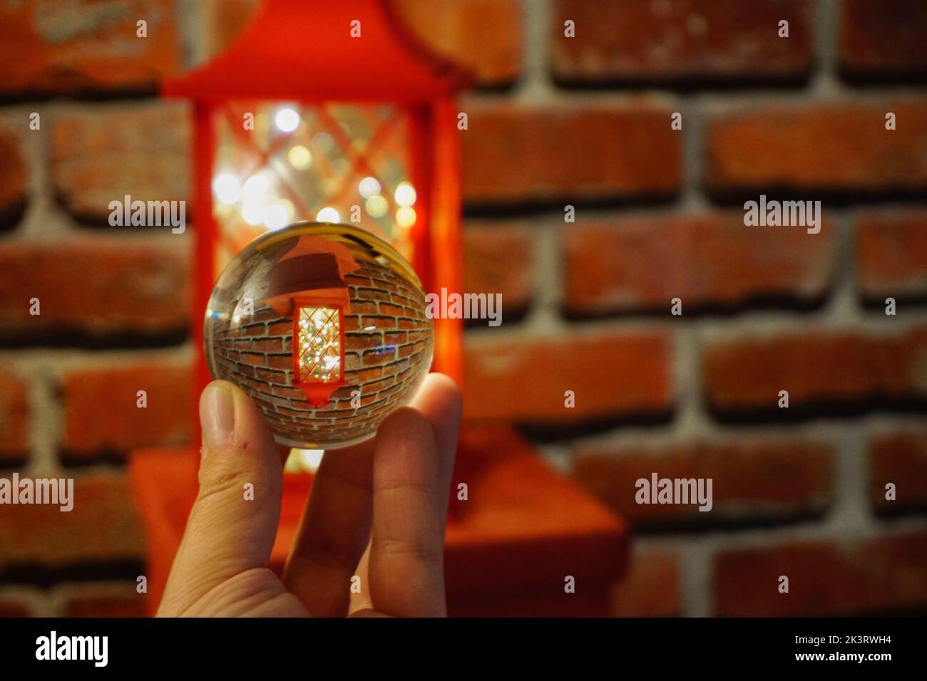 A glass sphere with reverse reflection in a hand against a brick ...