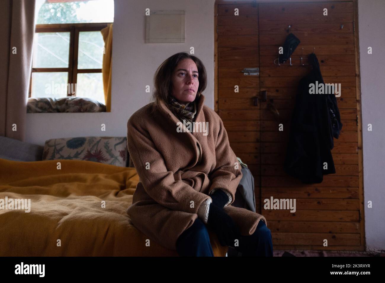 Woman wearing winter coat sits on a sofa bed in cabin while preparing ...