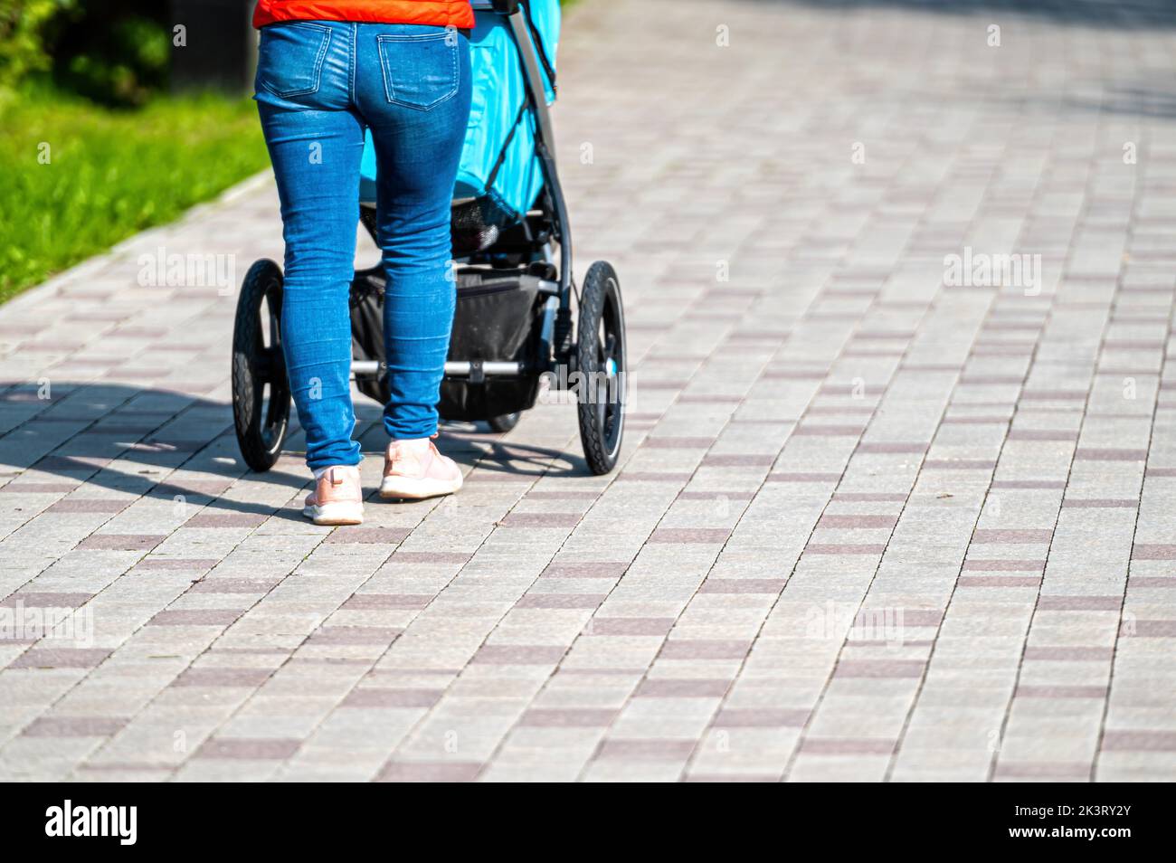 woman with baby carriage on paved path in city park, rear view, closeup ...