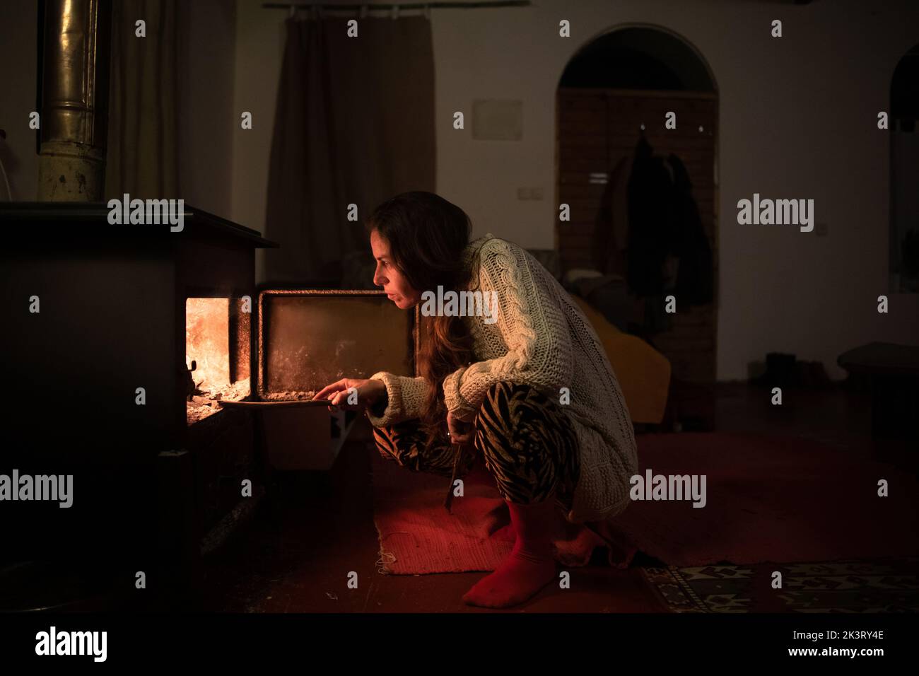 Woman burning firewood in a wood burning stove to heat a cabin during ...