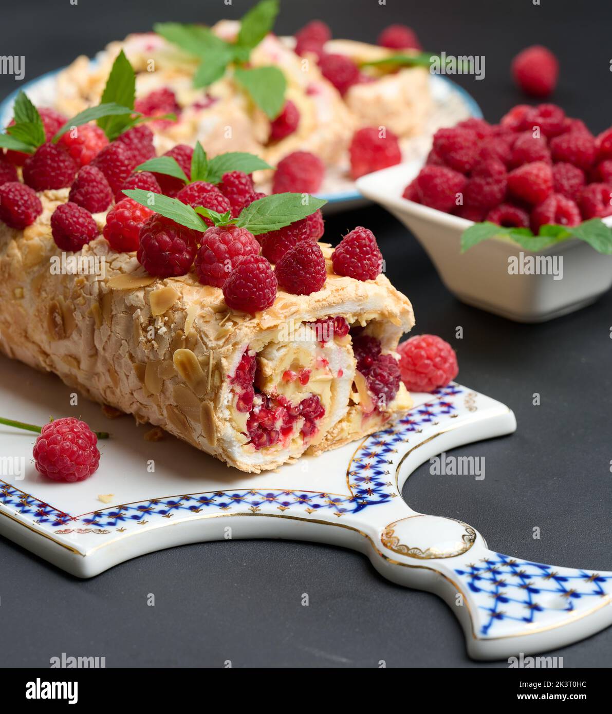 Baked meringue roll with cream and fresh red raspberry on a black ...