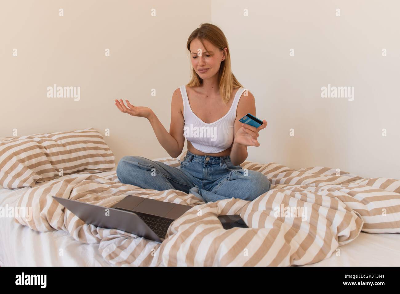 Upset woman holding credit card near laptop and smartphone on bed at ...