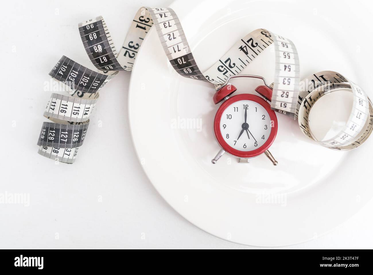 Intermittent fasting concept. Red alarm clock on an empty plate with ...