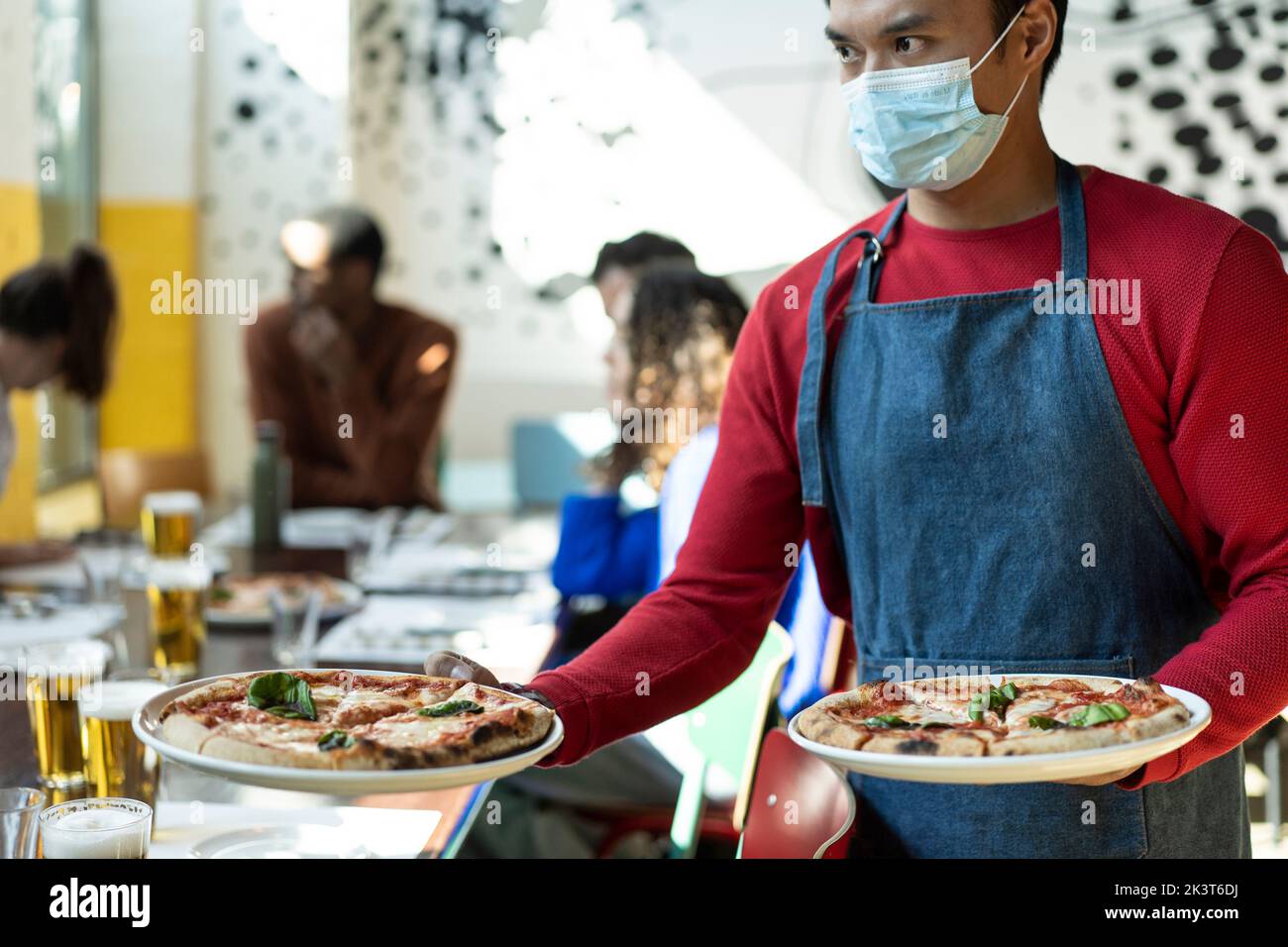 Waiter in protective face mask serving delicious pizza to friends in ...