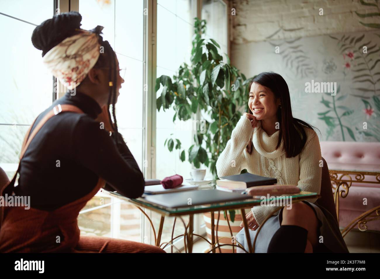 Two happy multicultural female college girls sit in the cafeteria ...
