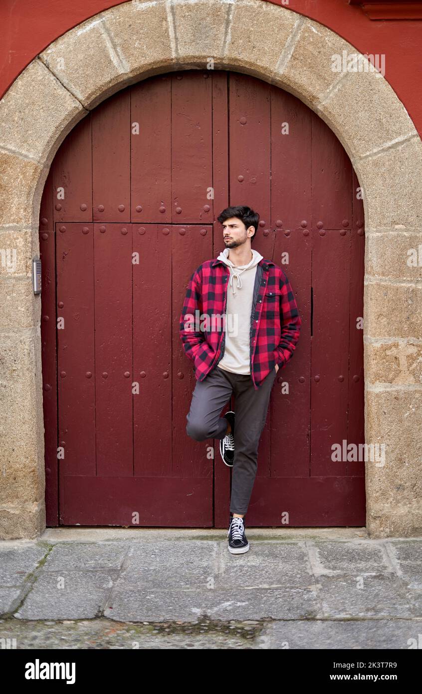 Serene male traveler with beard looking away while standing near red ...