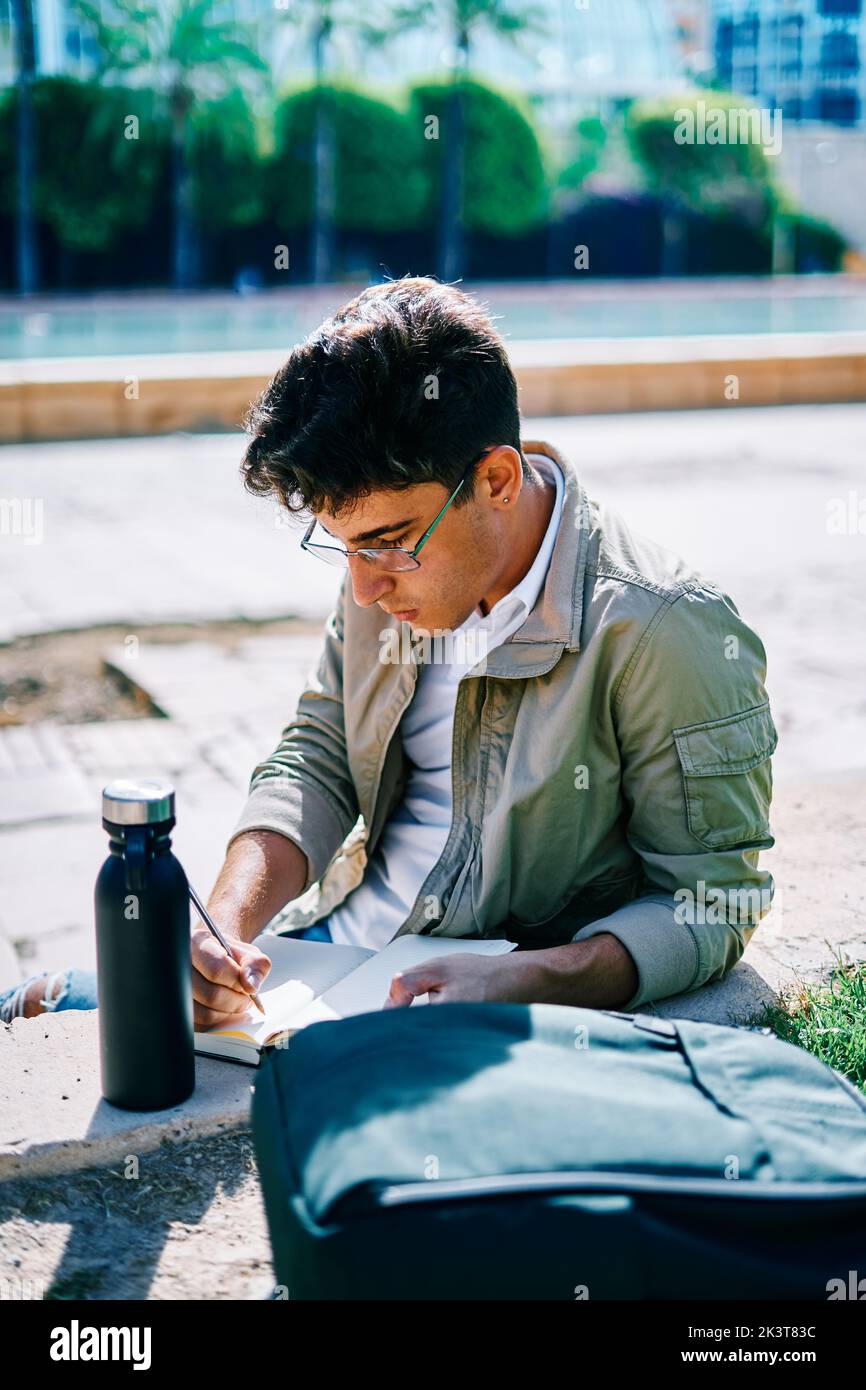 Focused male student sitting on stone bench in university campus and ...