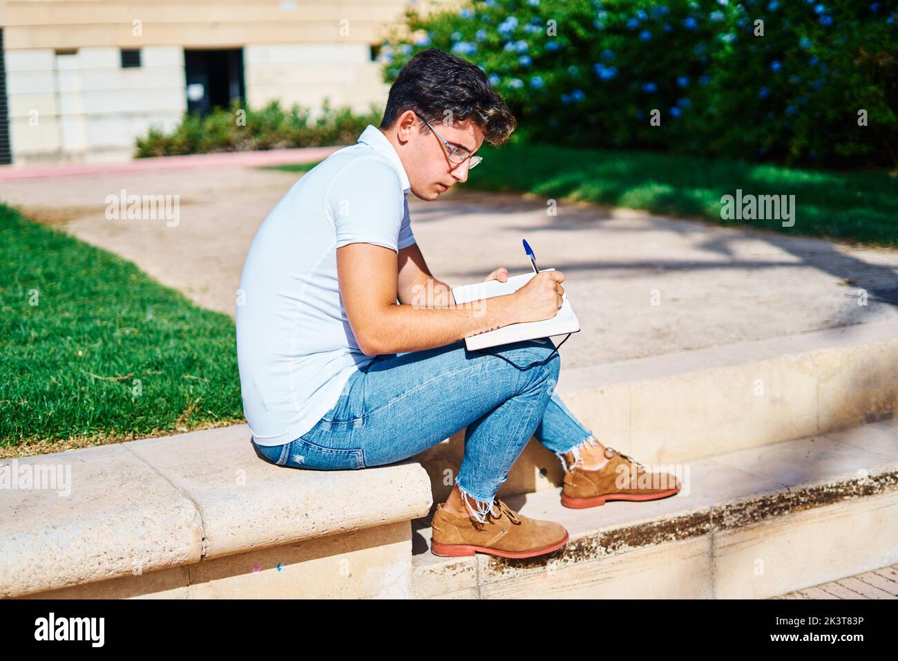 Side view of focused male student sitting on stone bench in university ...
