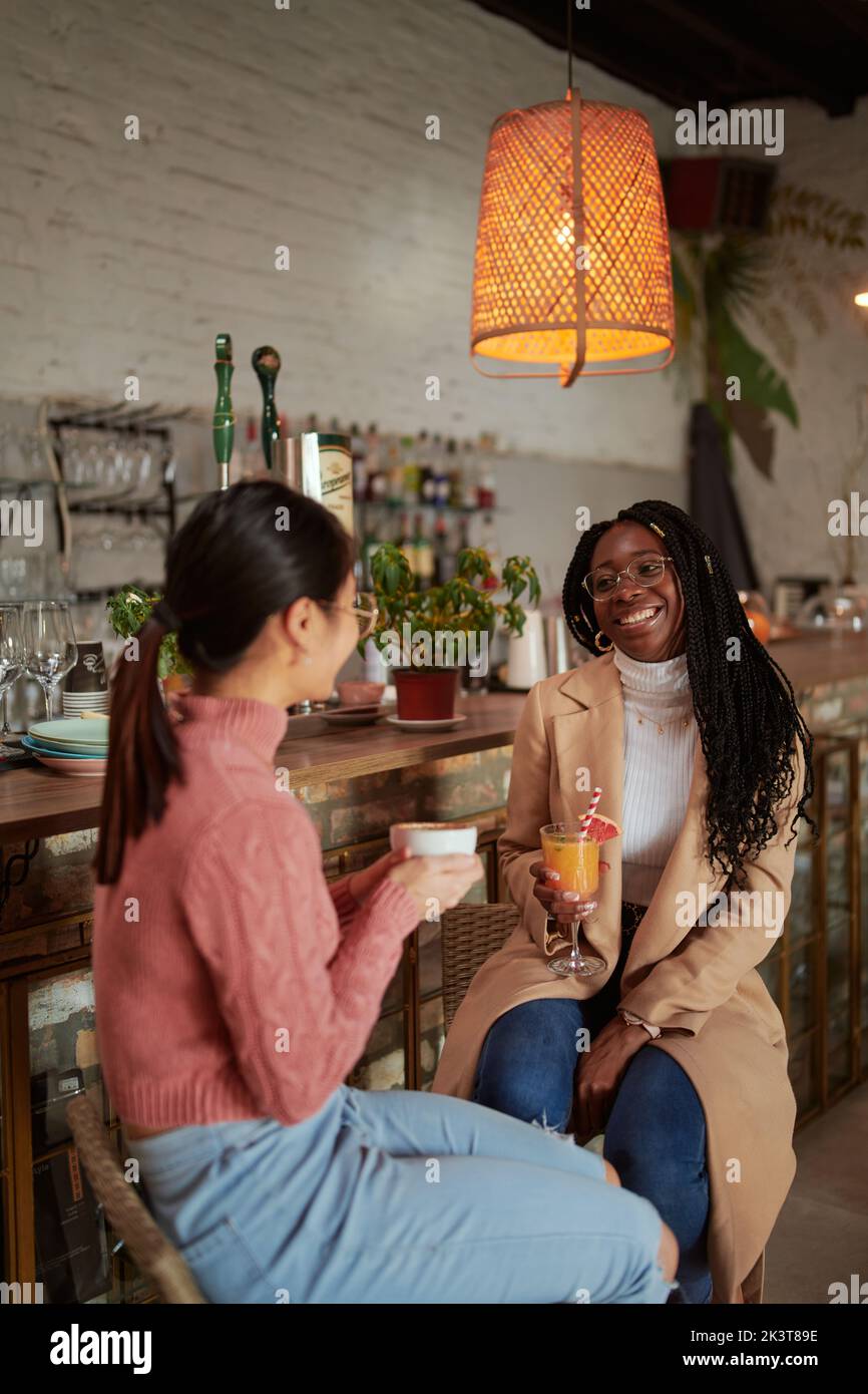 Two multicultural friends sit in the cafeteria, drink beverages, and ...