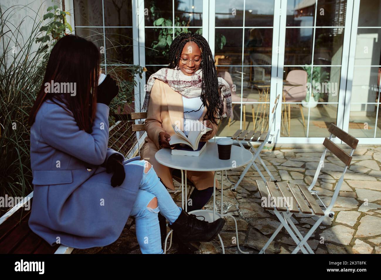 Two girls are sitting in a balcony of coffee shop, drinking coffee and ...