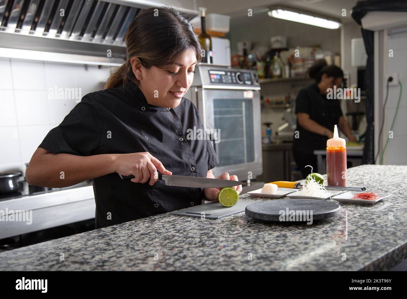 Focused hispanic female chef in uniform cutting green lime while ...